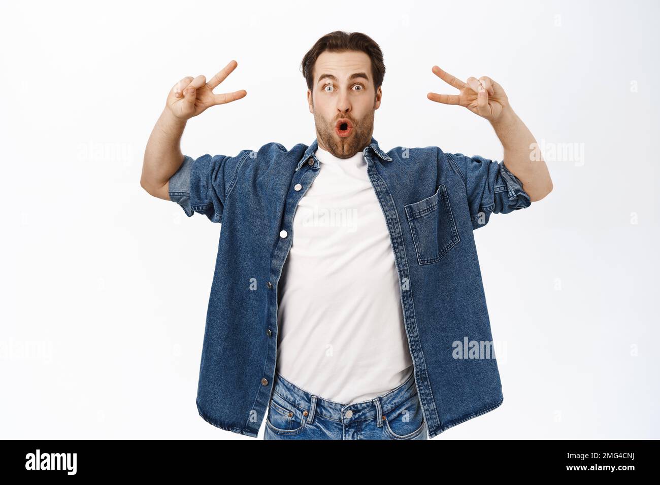 Positive handsome guy shows peace, v-signs and smiles happily, stands ...