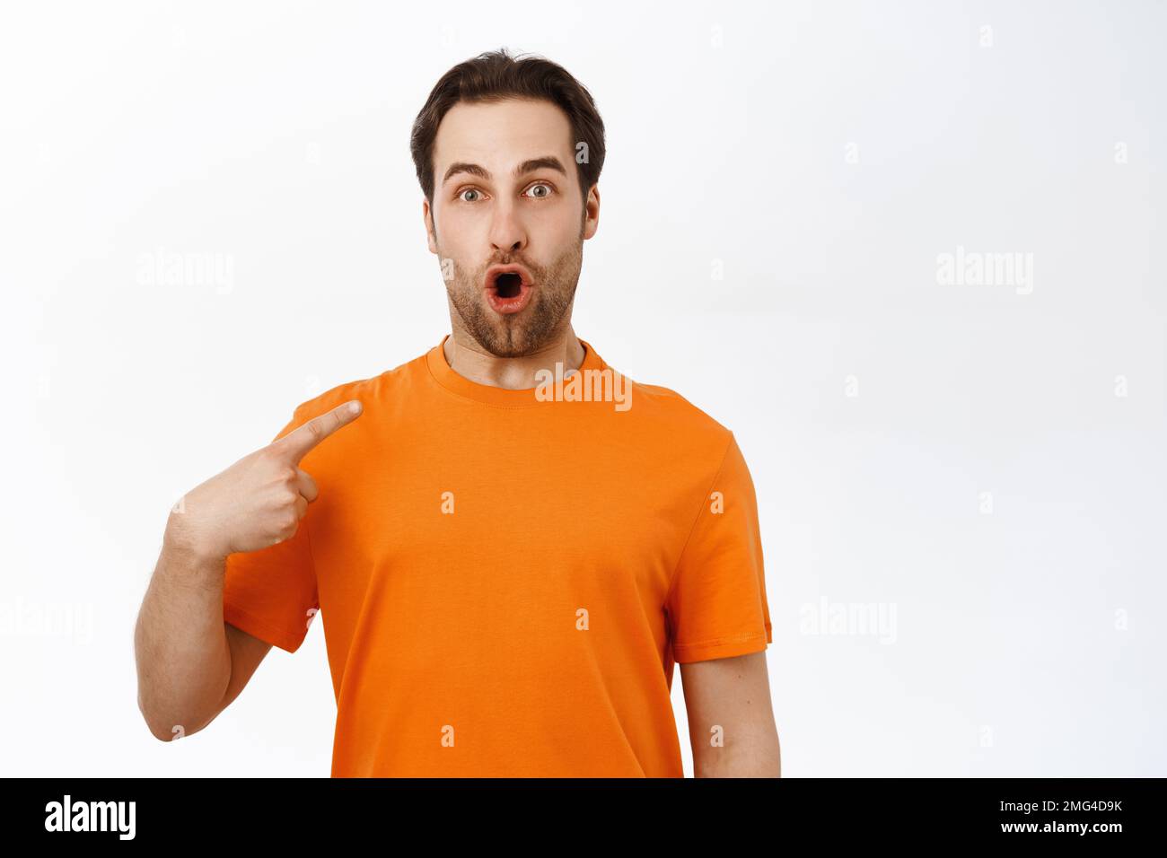 Portrait of young enthusiastic man looking surprised, pointing at ...