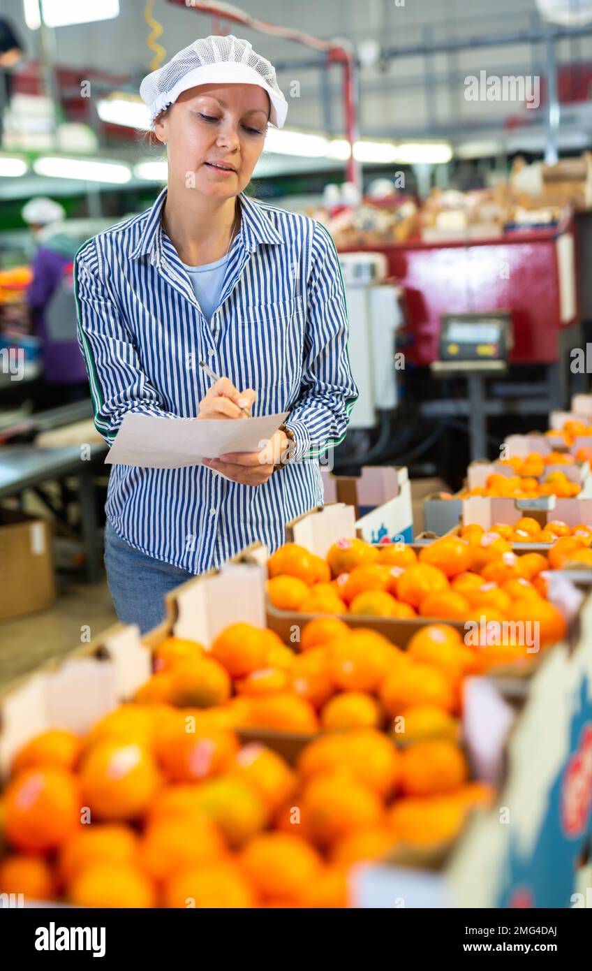 Positive female worker fills out a document at a citrus processing ...