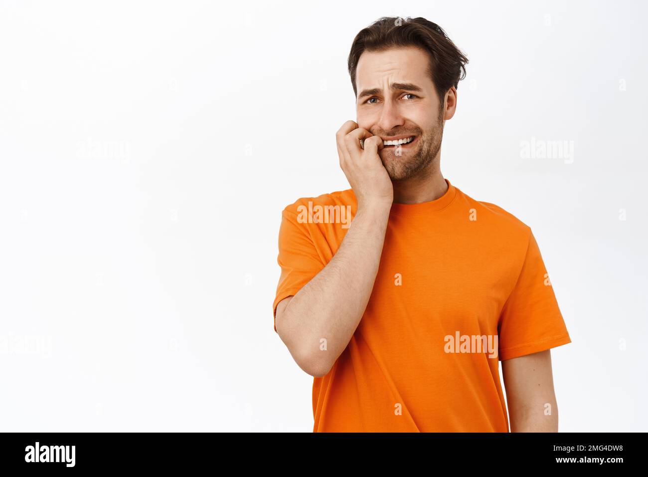 Scared adult man biting his fingernails, looking anxious, standing over ...