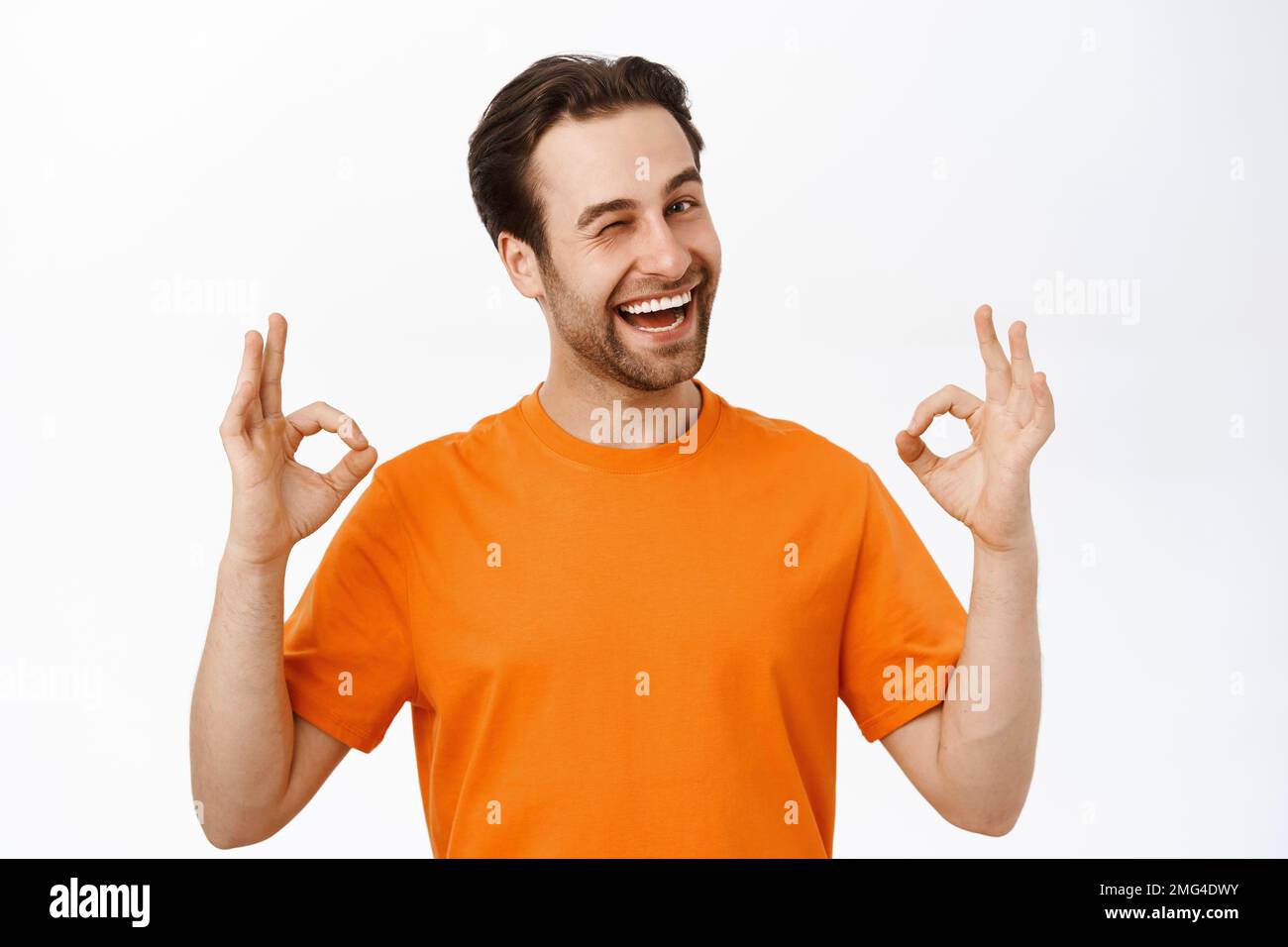 Portrait of handsome happy guy shows okay sign, stands in orange tshirt ...