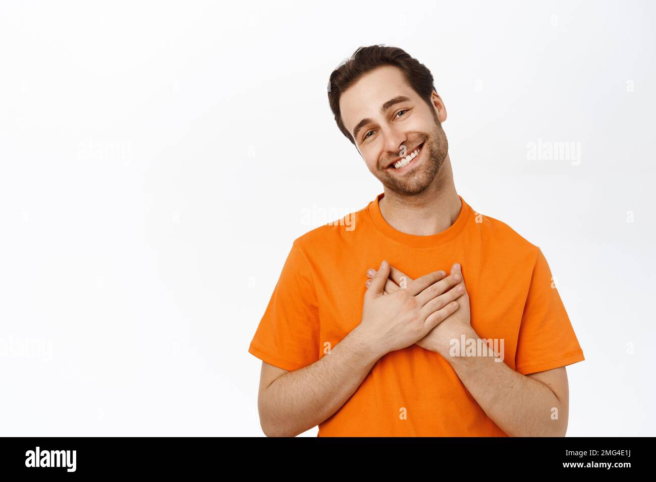 Cute smiling man holds hands on heart and looks delighted, stands in ...