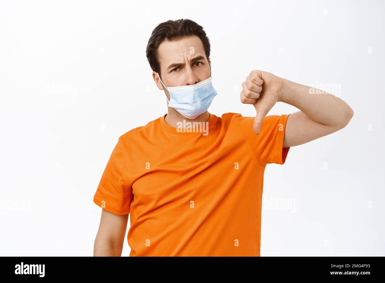 Portrait of guy wears medical face mask wrong and shows thumbs down ...
