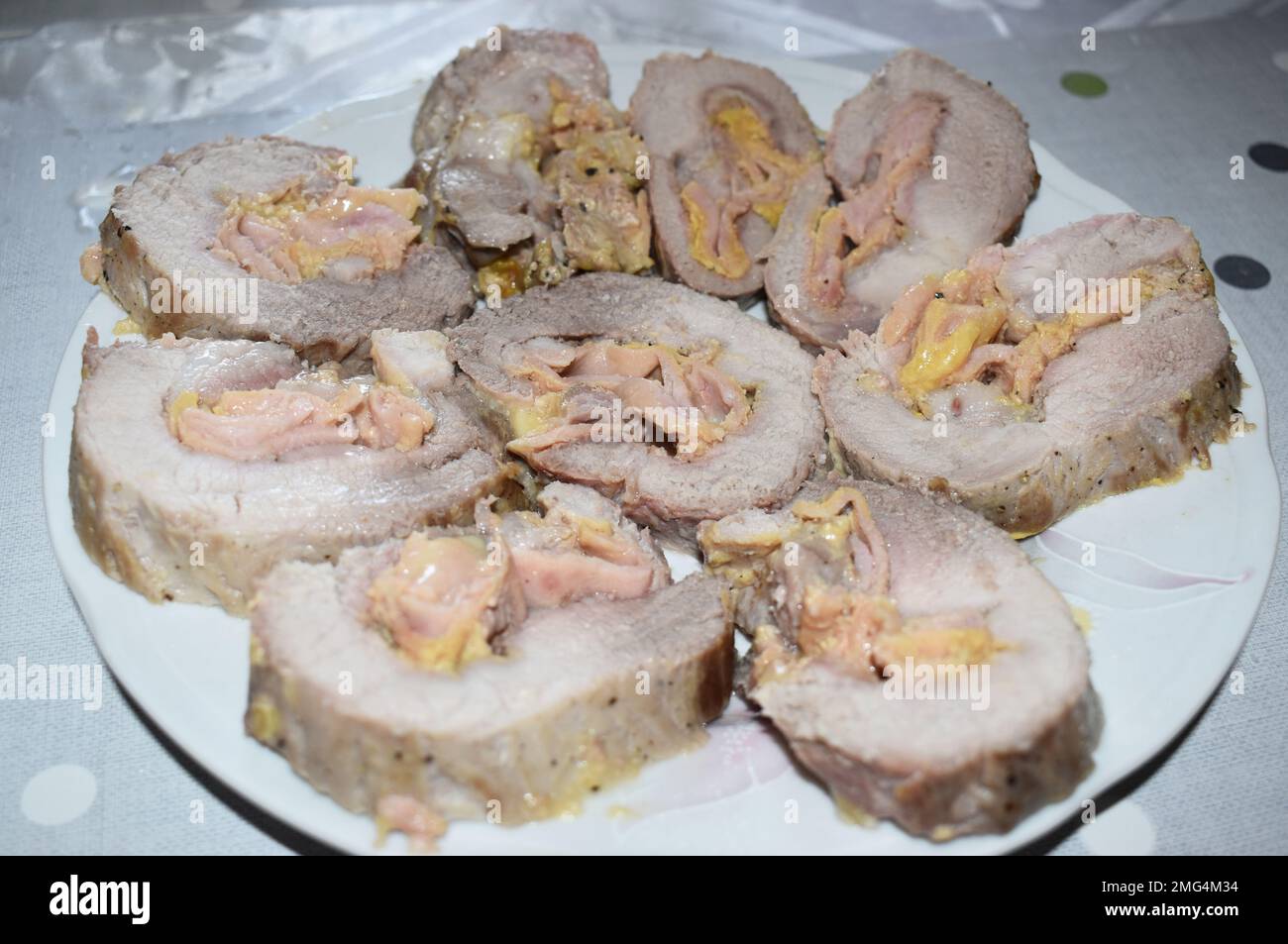 Close up of rolled pork roast served on a big white plate on a grey ...