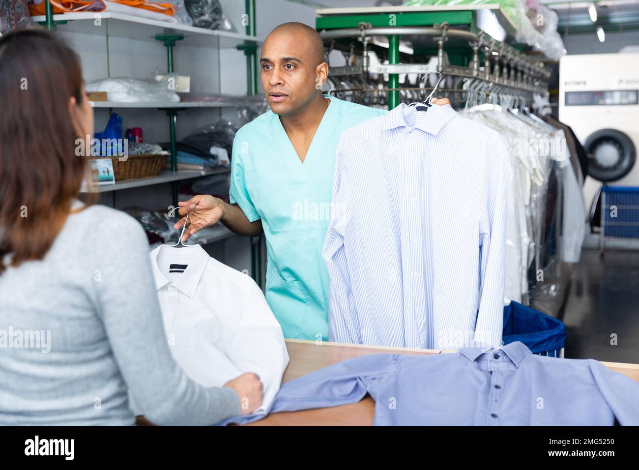 Laundry employee handing out clean clothes to client Stock Photo - Alamy