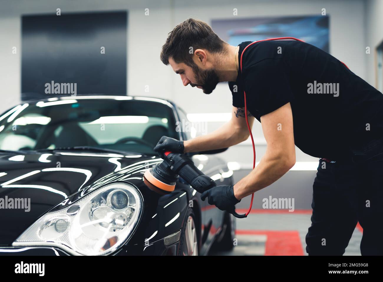Caucasian man leaning over the front of black car using professional ...
