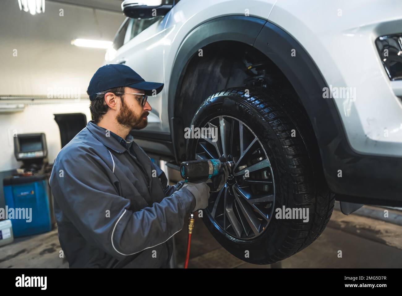 Medium shot of a mechanic fixing a car wheel in a repair shop. High ...