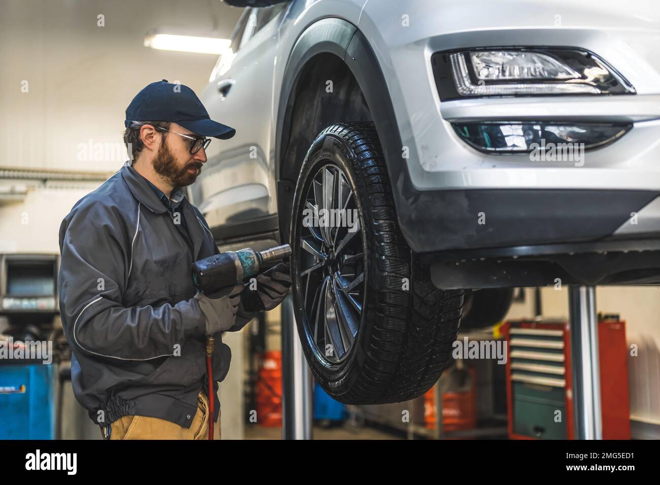 Medium shot of a mechanic standing by a car held on a lift and ...