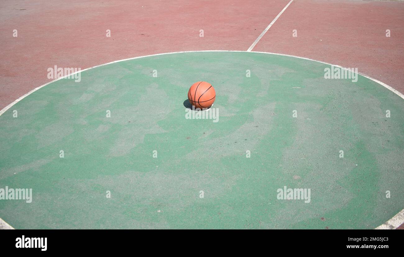 Part of red and green concrete basketball court and orange ball on it ...
