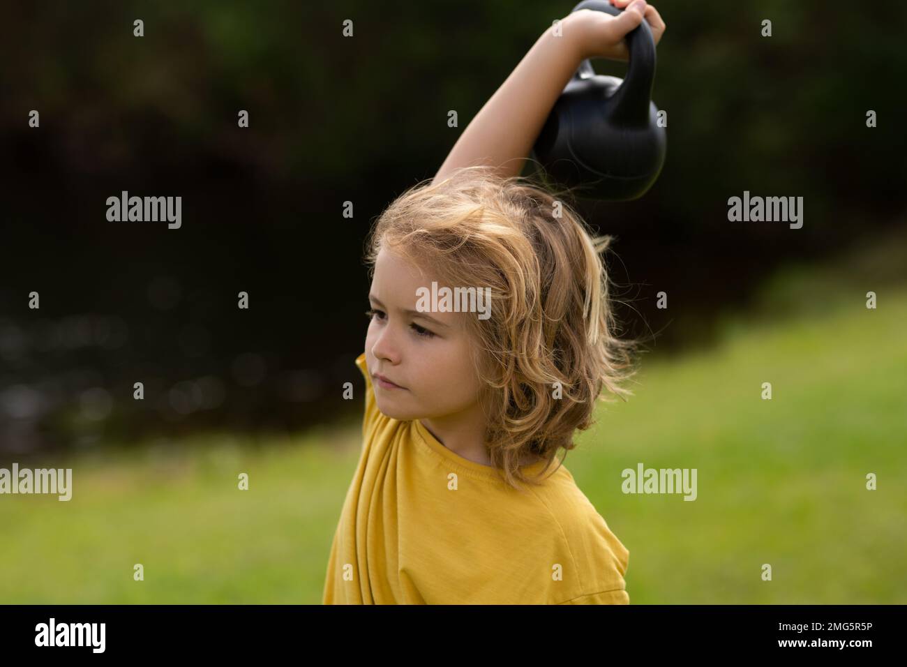 Kid lifting the kettlebell in park outside. Child boy raising a ...