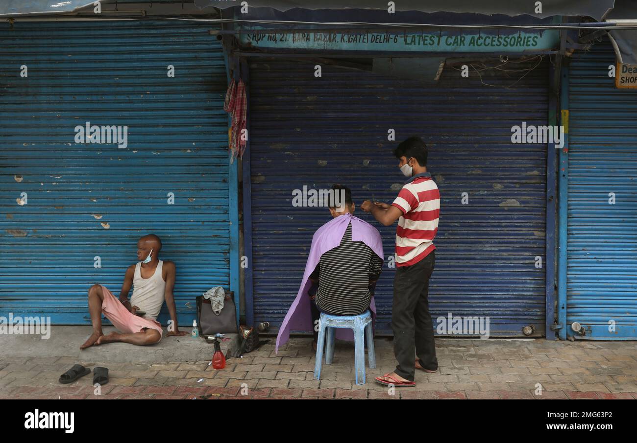 A roadside barber gives haircut to a daily wage laborer outside a ...