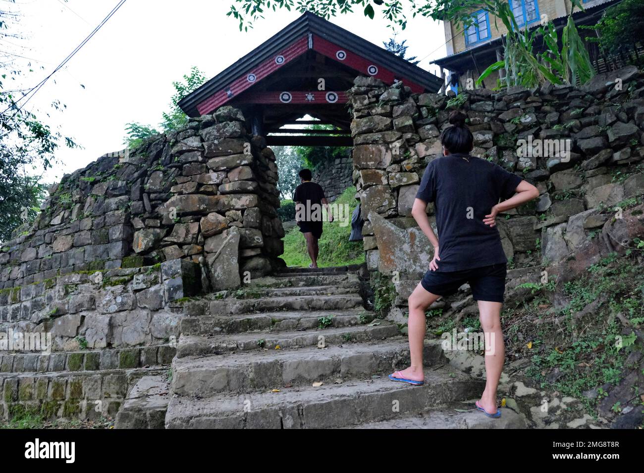 A woman rests by a flight of stairs in front of a traditional Naga ...