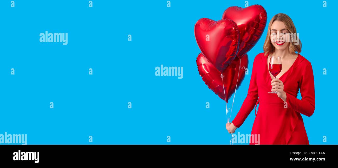Beautiful young woman with heart-shaped balloons and wine on blue ...