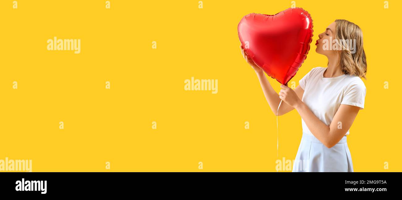 Beautiful young woman with heart-shaped balloon on yellow background ...