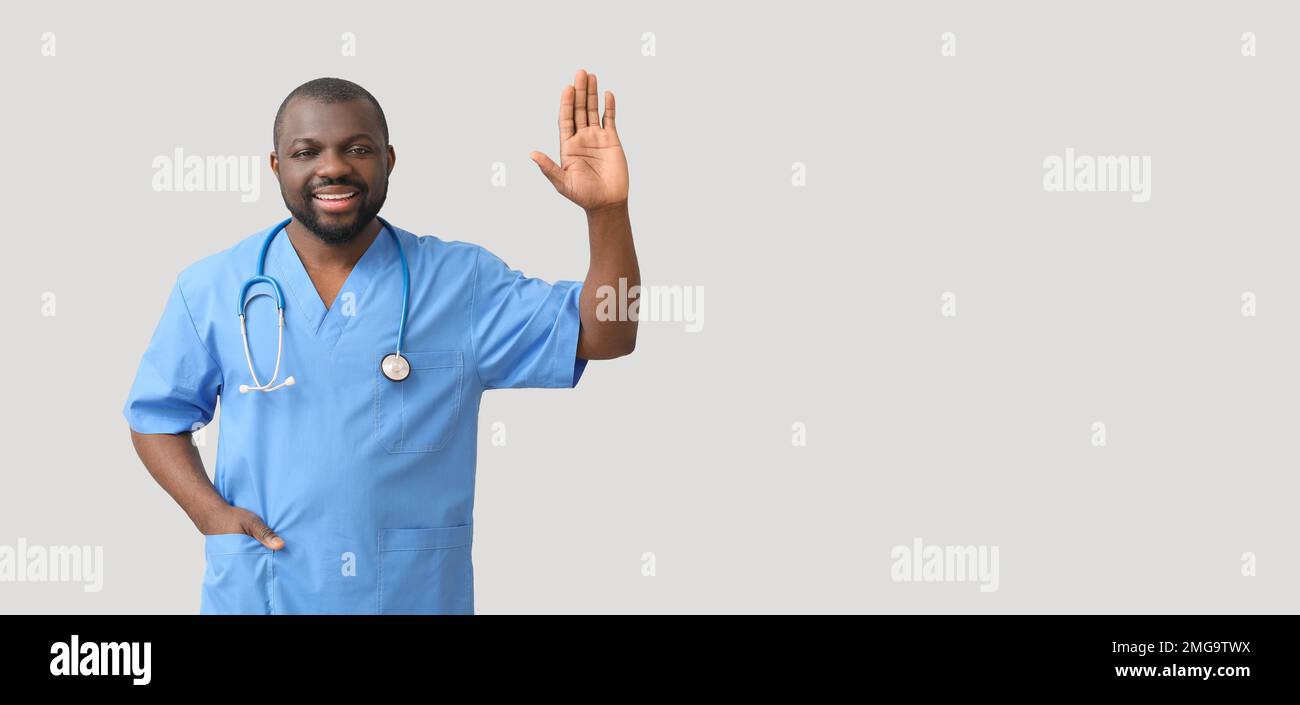 African-American doctor waving hand on light background with space for ...