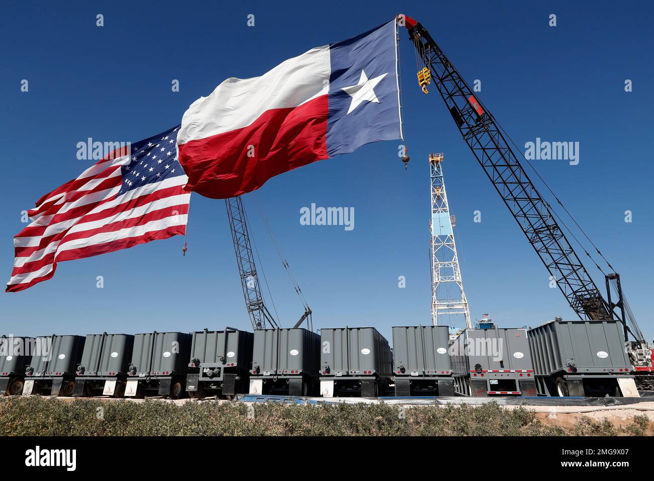 An American and Texas flag fly from the tops of cranes near an oil rig ...