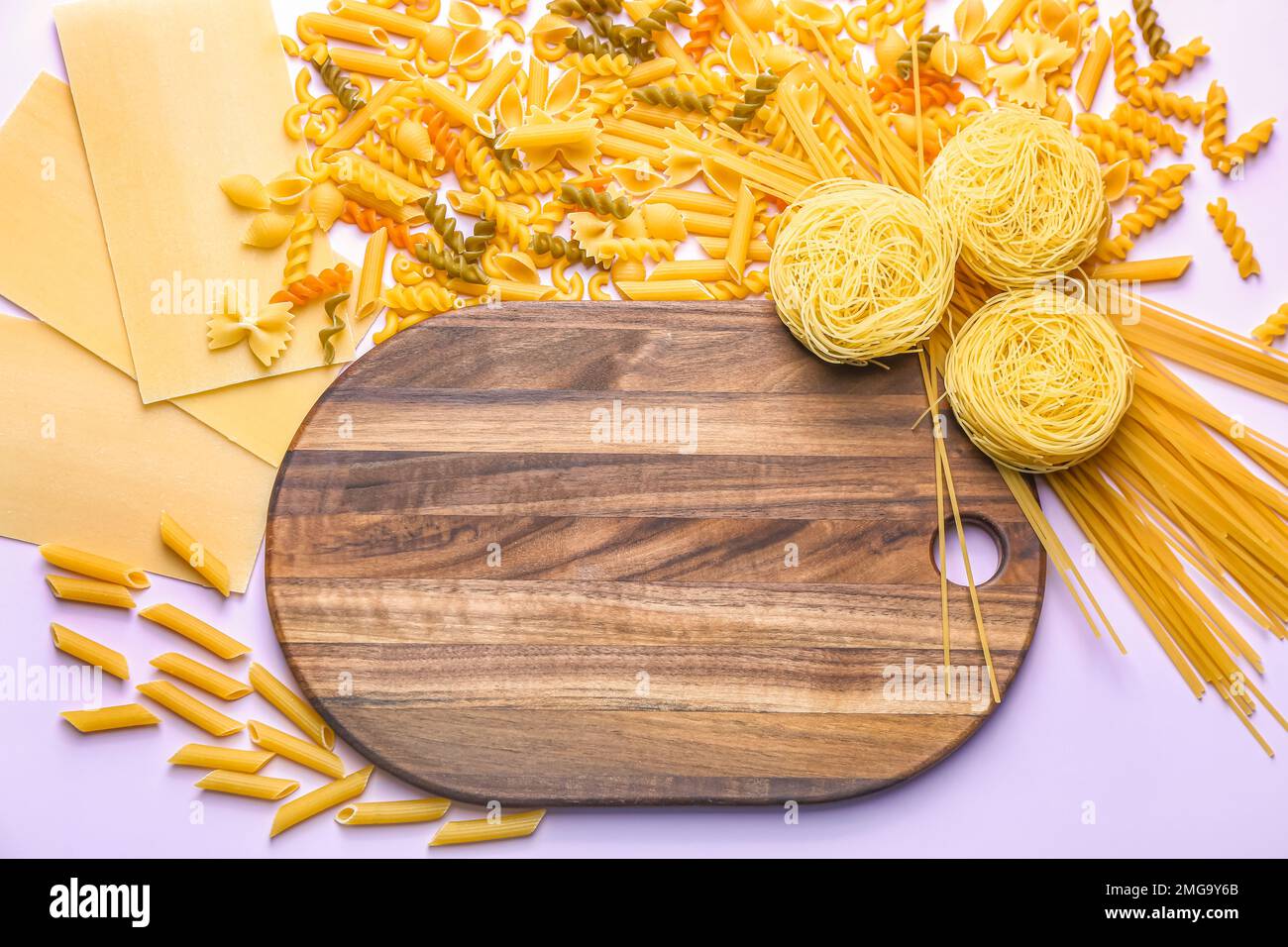 Wooden board and different types of raw pasta on lilac background Stock ...