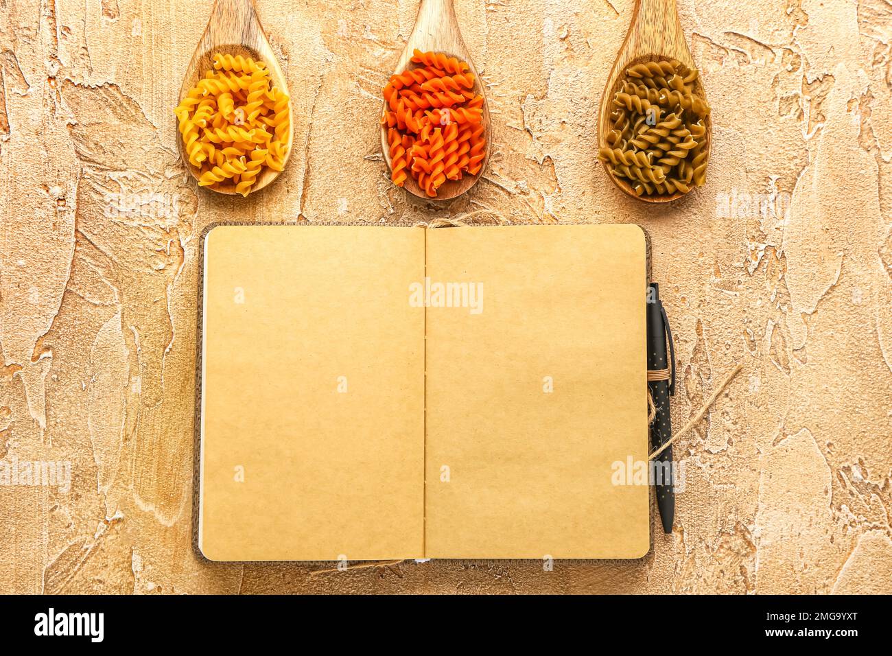Blank notebook and spoons with raw pasta on color background Stock ...