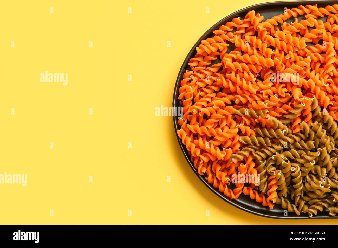 Plate with raw fusilli pasta on yellow background Stock Photo - Alamy