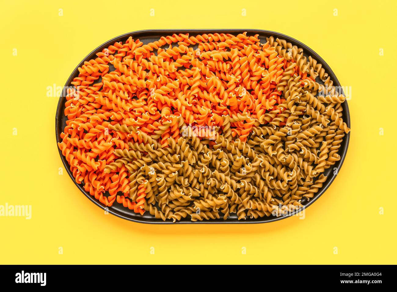 Plate with raw fusilli pasta on yellow background Stock Photo - Alamy