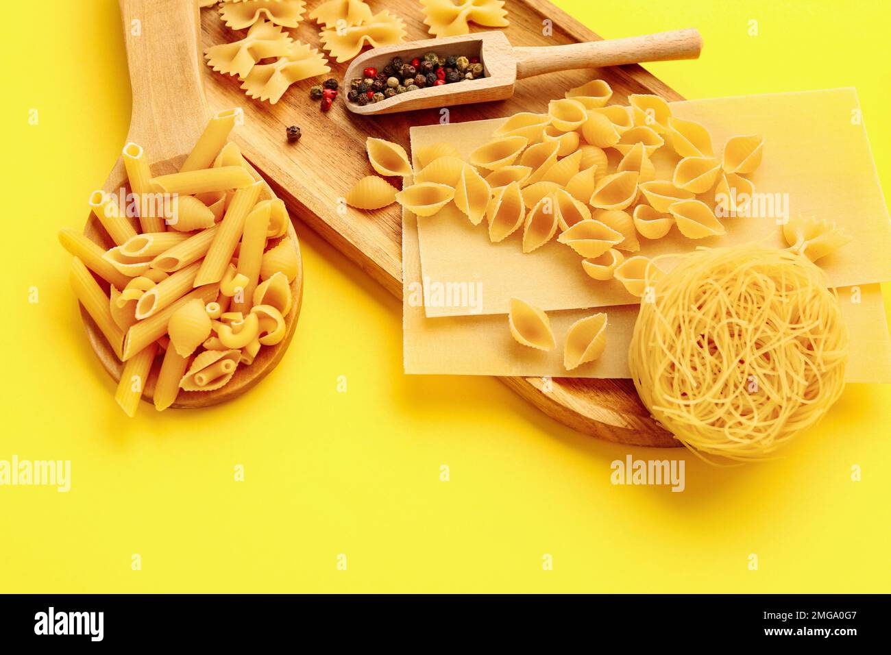 Wooden board with different types of raw pasta on yellow background ...