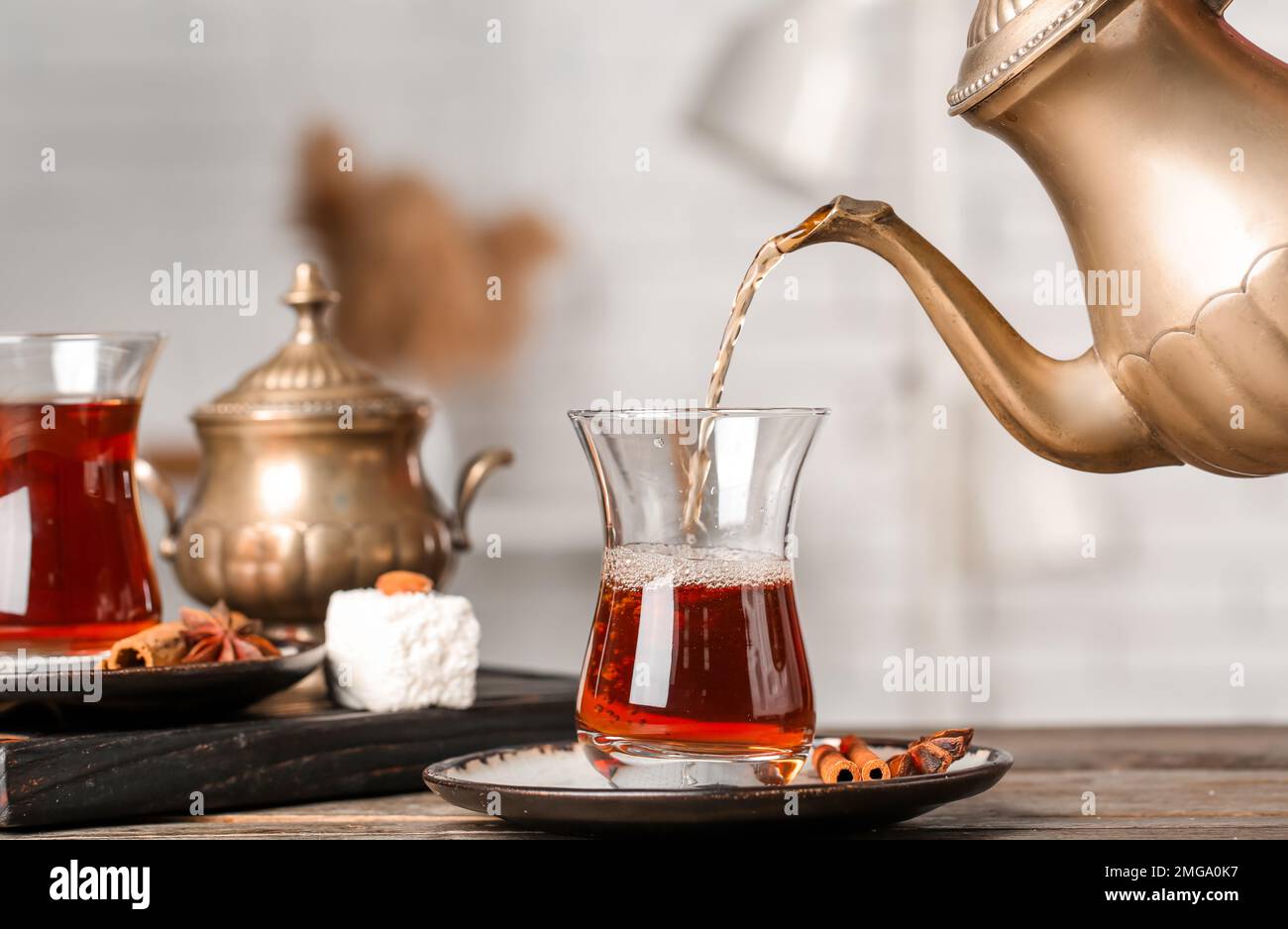 Pouring of hot Turkish tea from teapot into glass on wooden table ...