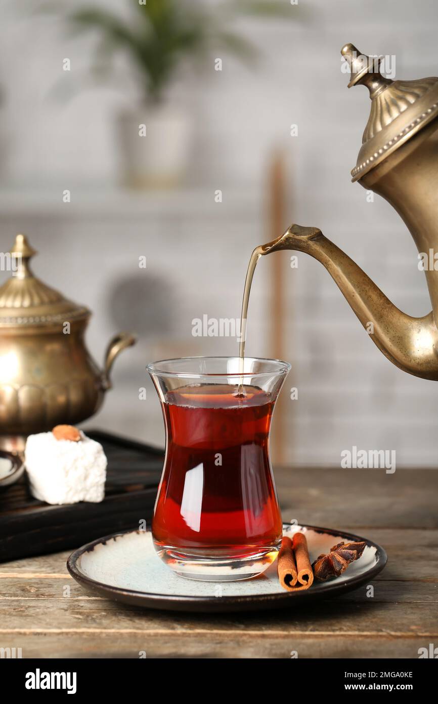Pouring of hot Turkish tea from teapot into glass on wooden table ...