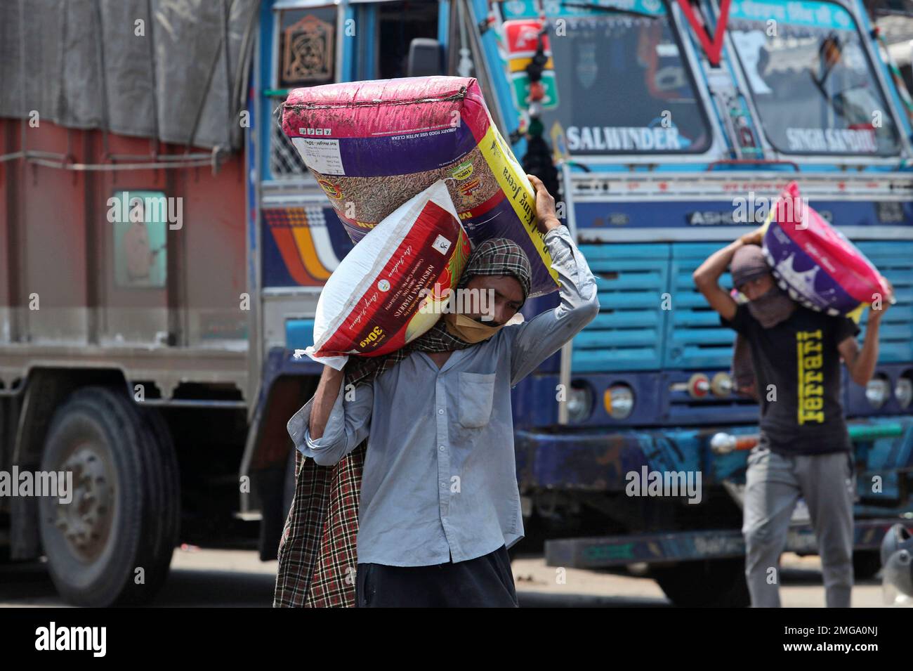 Laborers wearing face masks carry sacks of food at a warehouse in Jammu ...