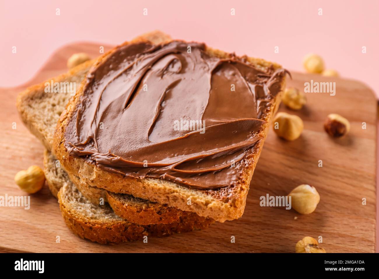 Wooden board of tasty toasts with hazelnut butter on pink background ...