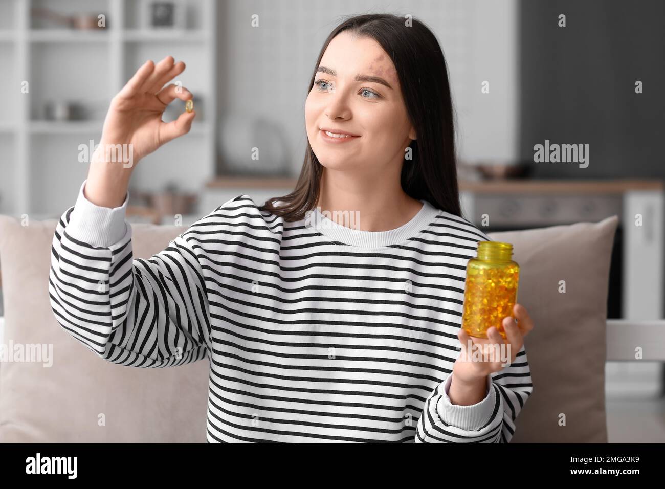 Young woman taking vitamin supplement from bottle at home Stock Photo ...