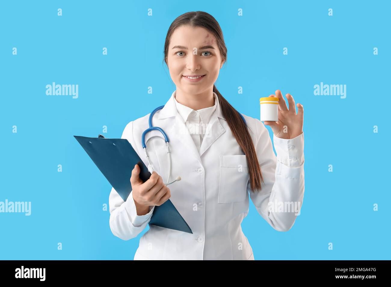 Female doctor with bottle of vitamin supplements and clipboard on blue ...