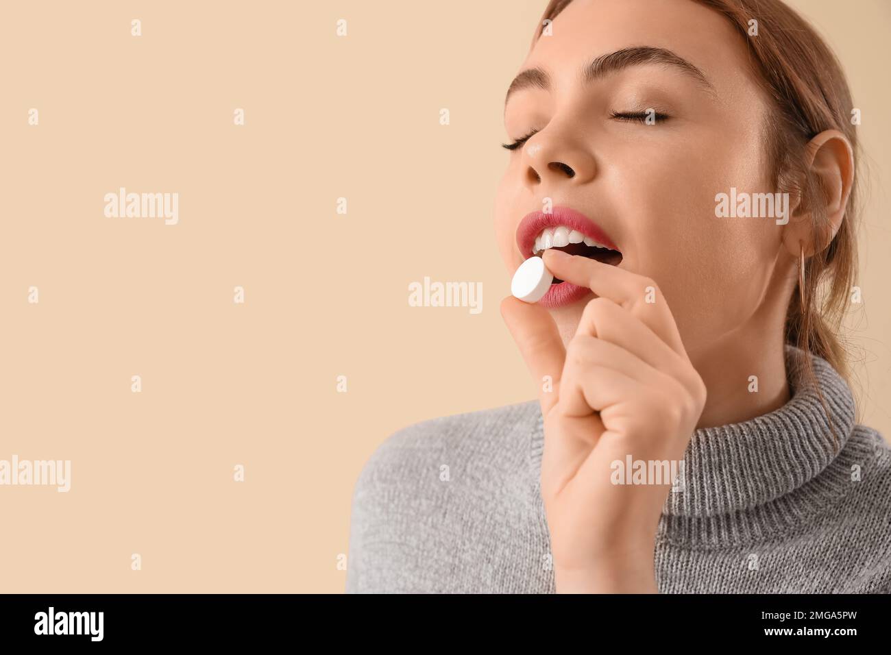 Beautiful young woman taking vitamin supplement on beige background ...
