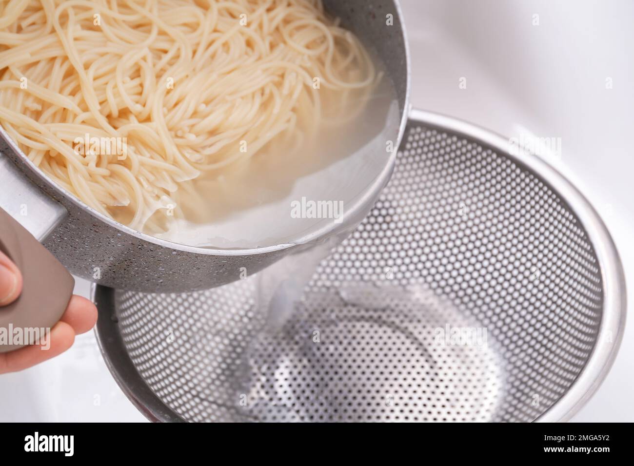 Woman pouring water from boiled pasta over sink, closeup Stock Photo ...