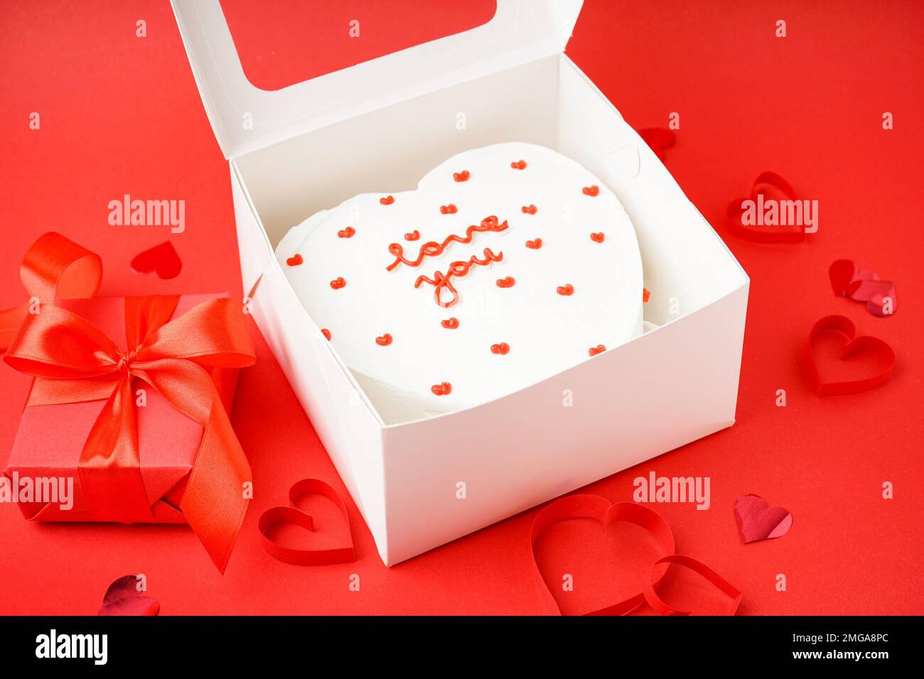 Opened box with heart-shaped bento cake and gift on red background ...