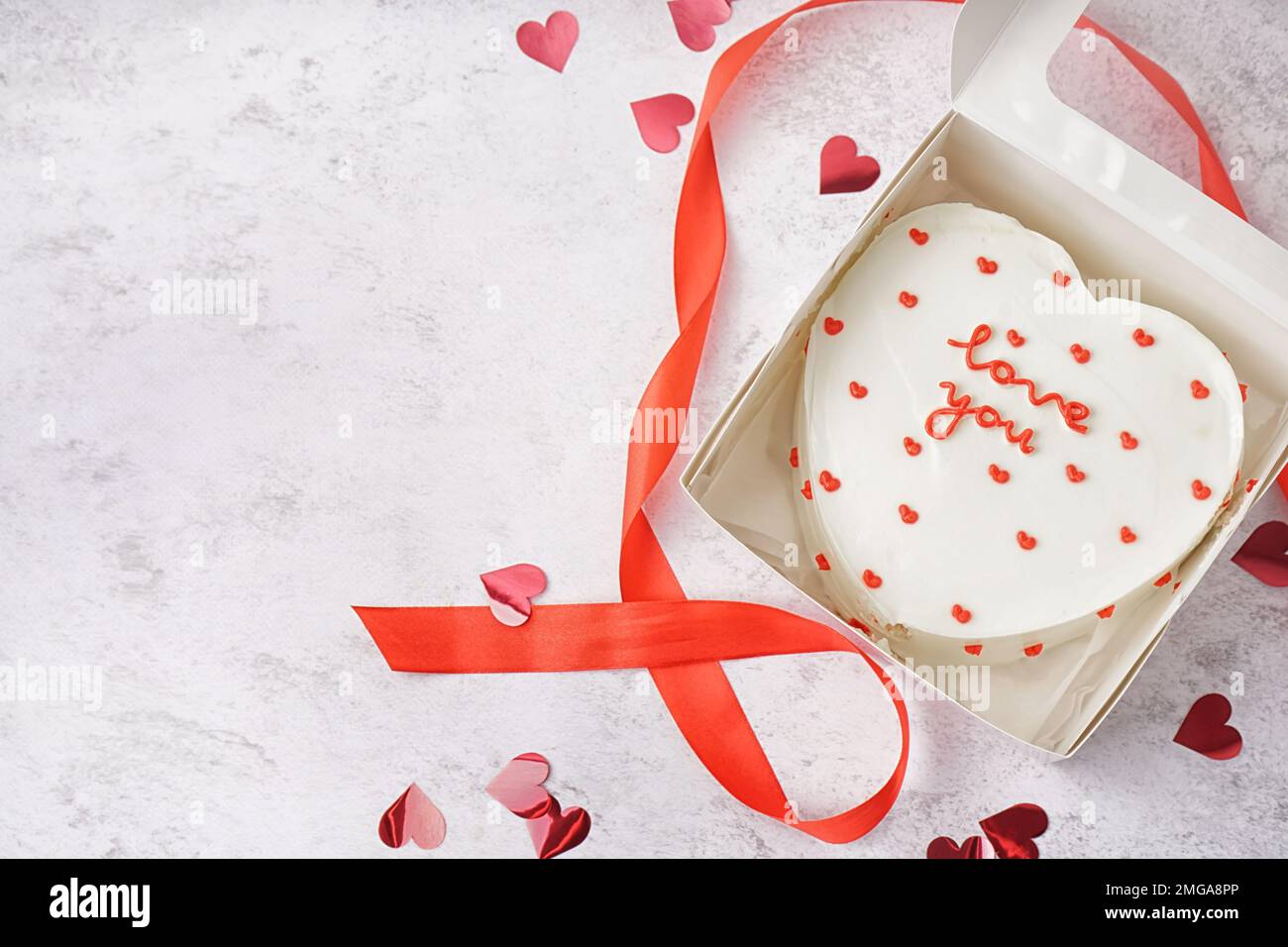 Box with heart-shaped bento cake and ribbon on white background ...
