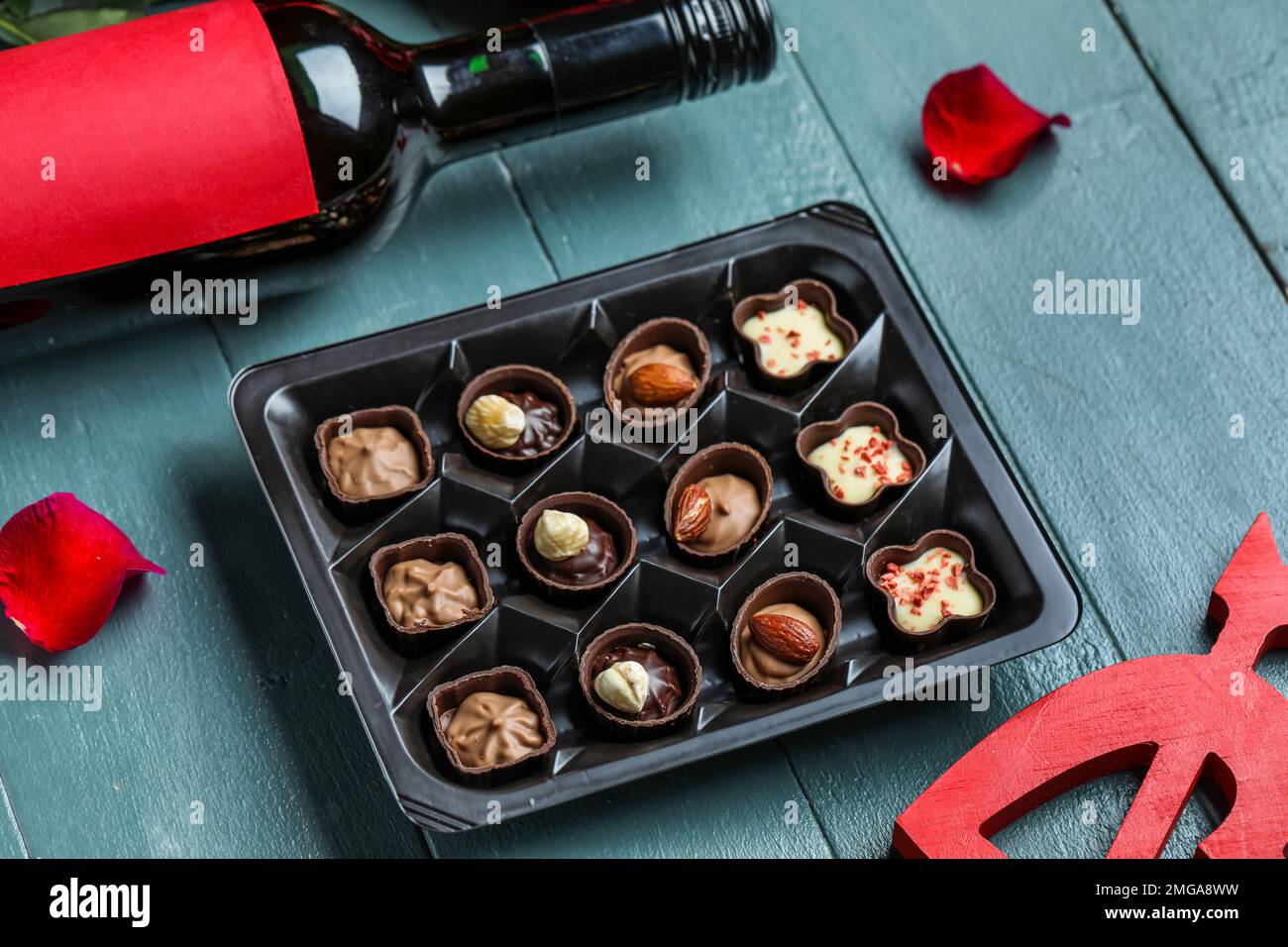 Box with candies, bottle of wine and rose petals on grey wooden ...