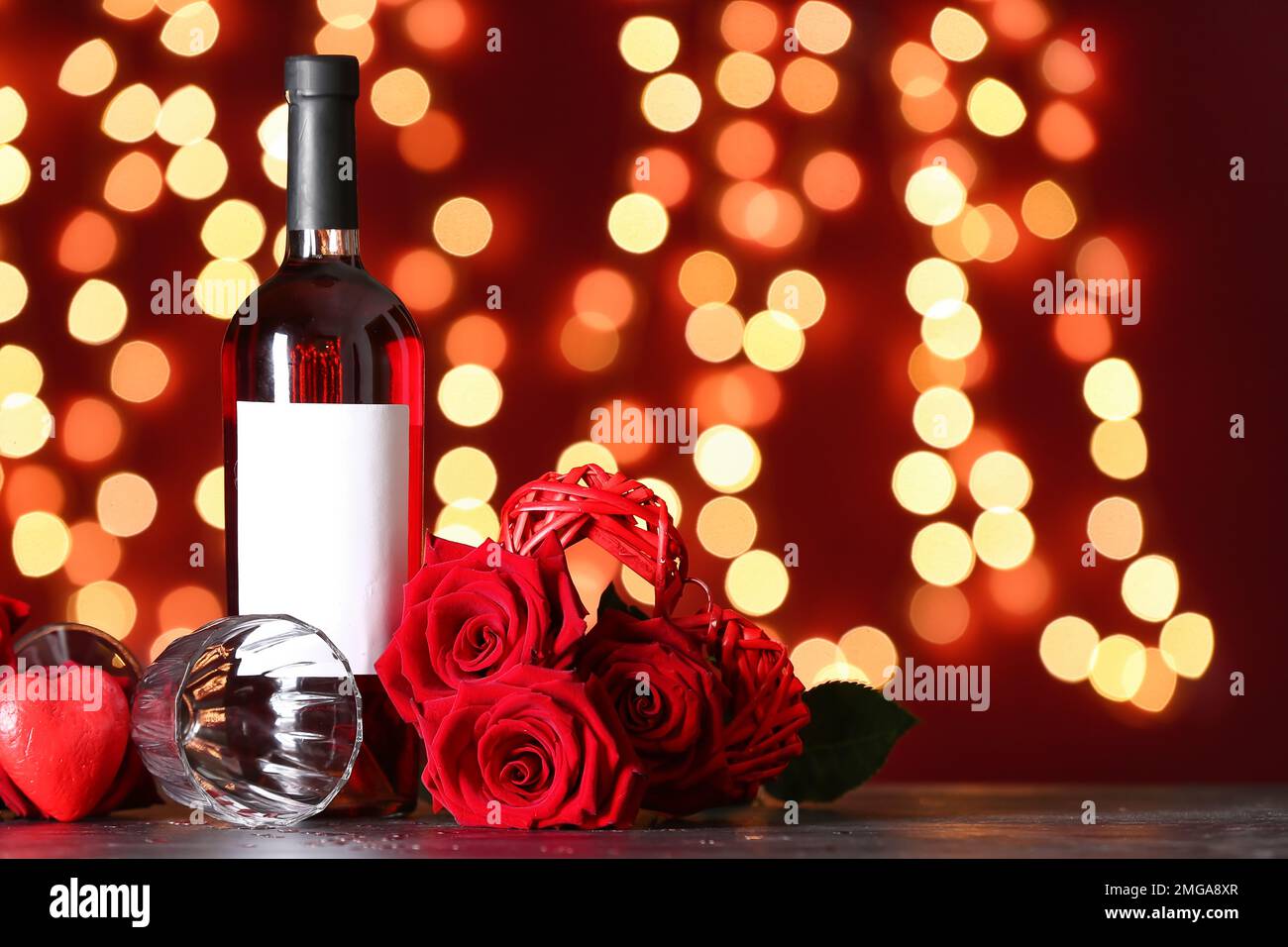 Bottle of wine, glass and rose flowers on table against blurred lights ...