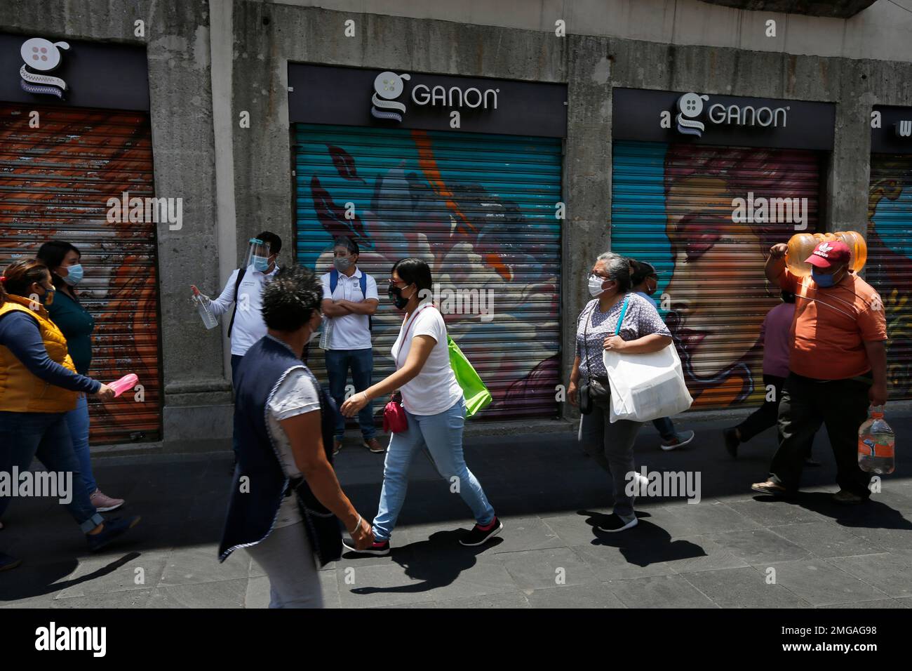 Pedestrians, wearing protective face masks, walk past a shuttered ...