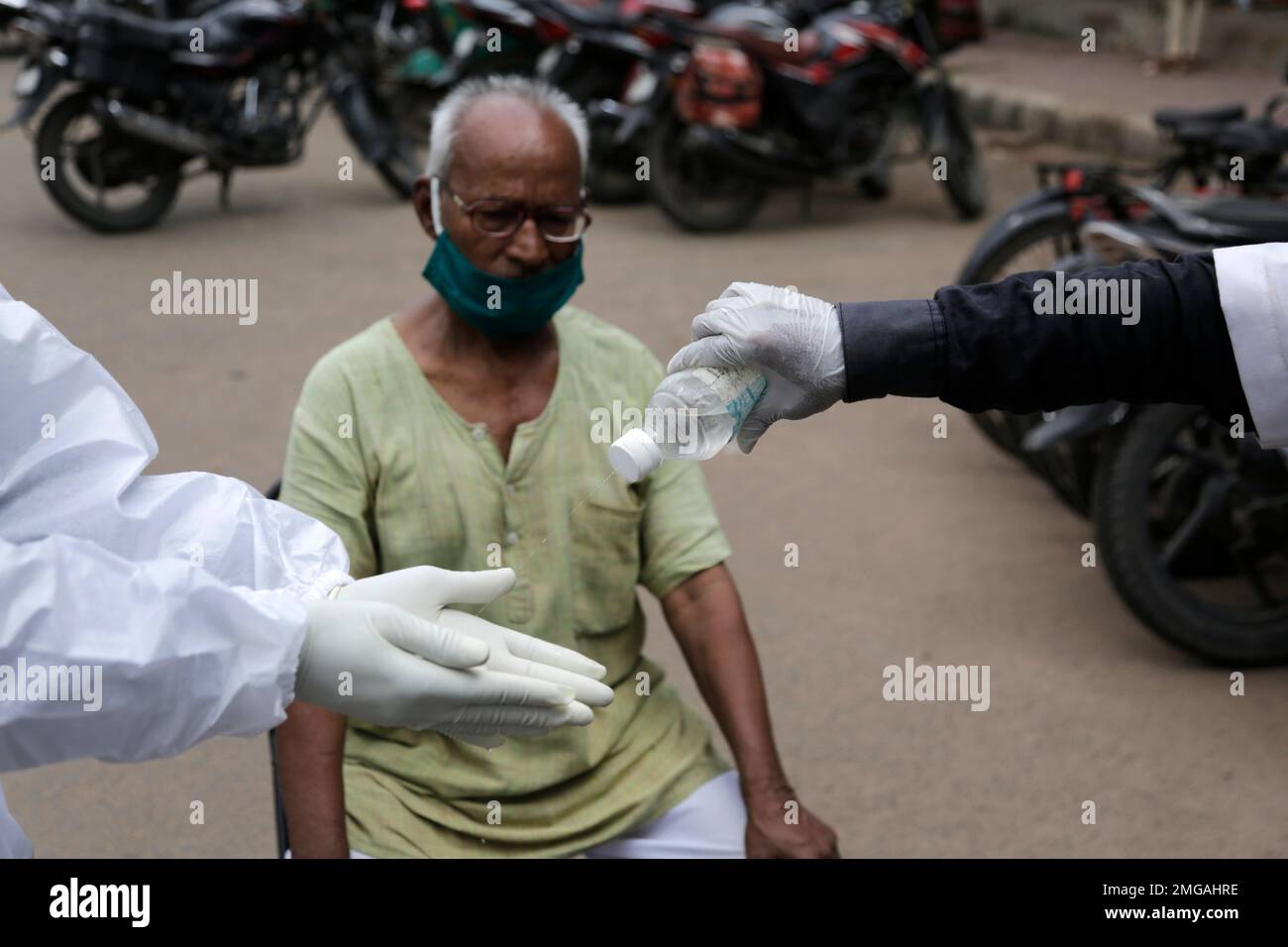 An Indian health worker sprays sanitizer to other's hands after taking ...