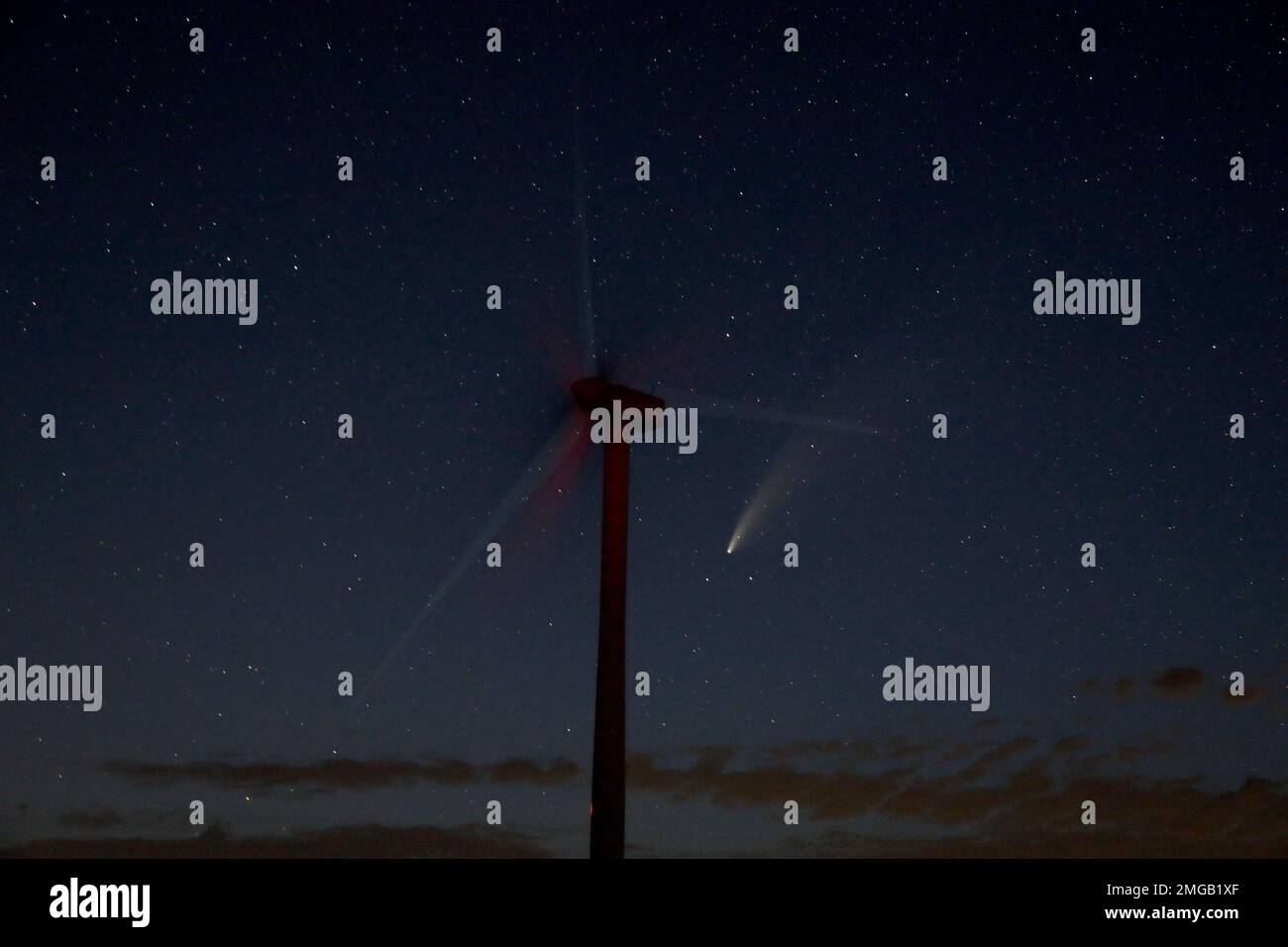 The comet Neowise is seen in the night sky beyond a wind turbine ...