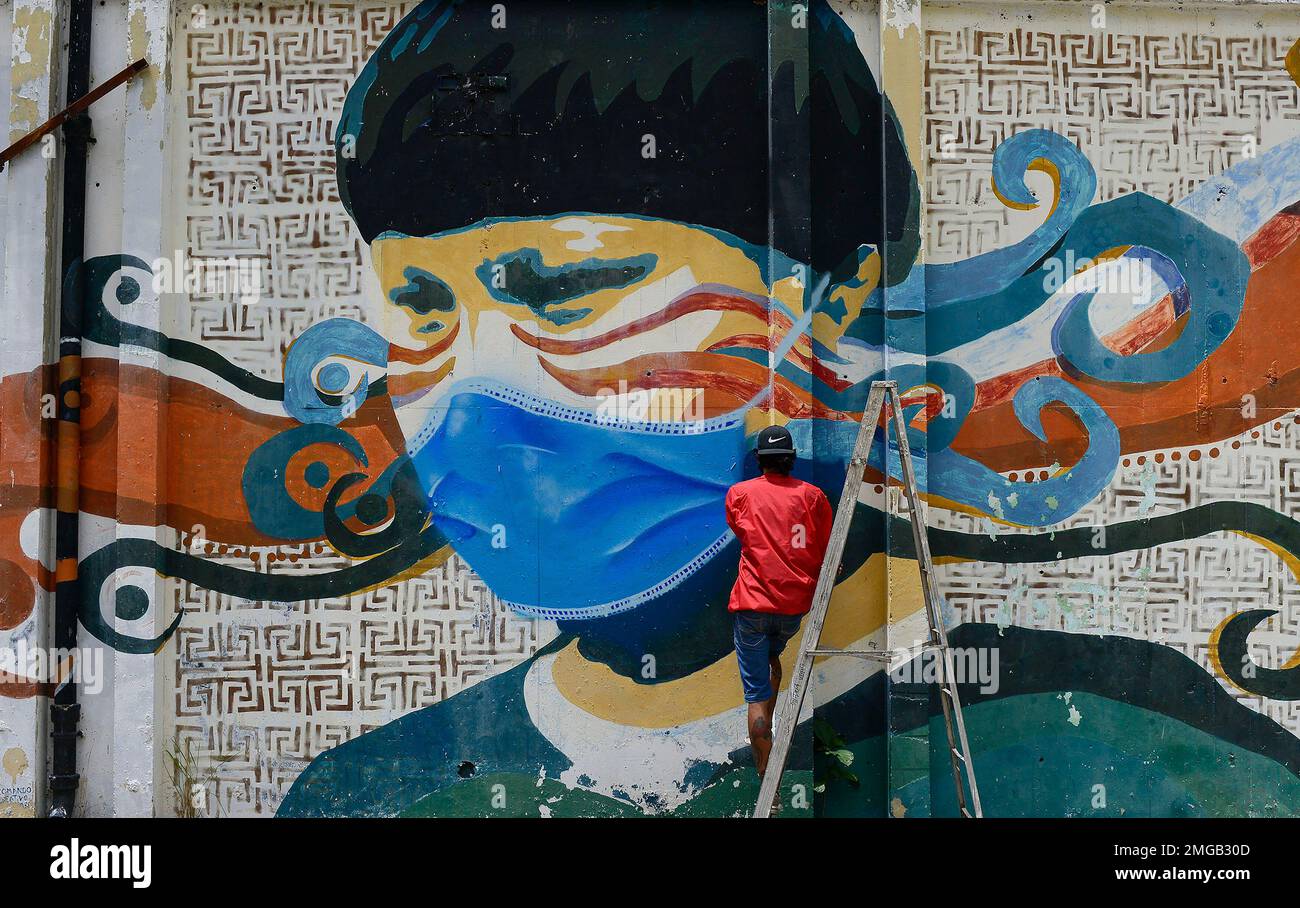A street artist spray paints a protective face mask over an old mural ...