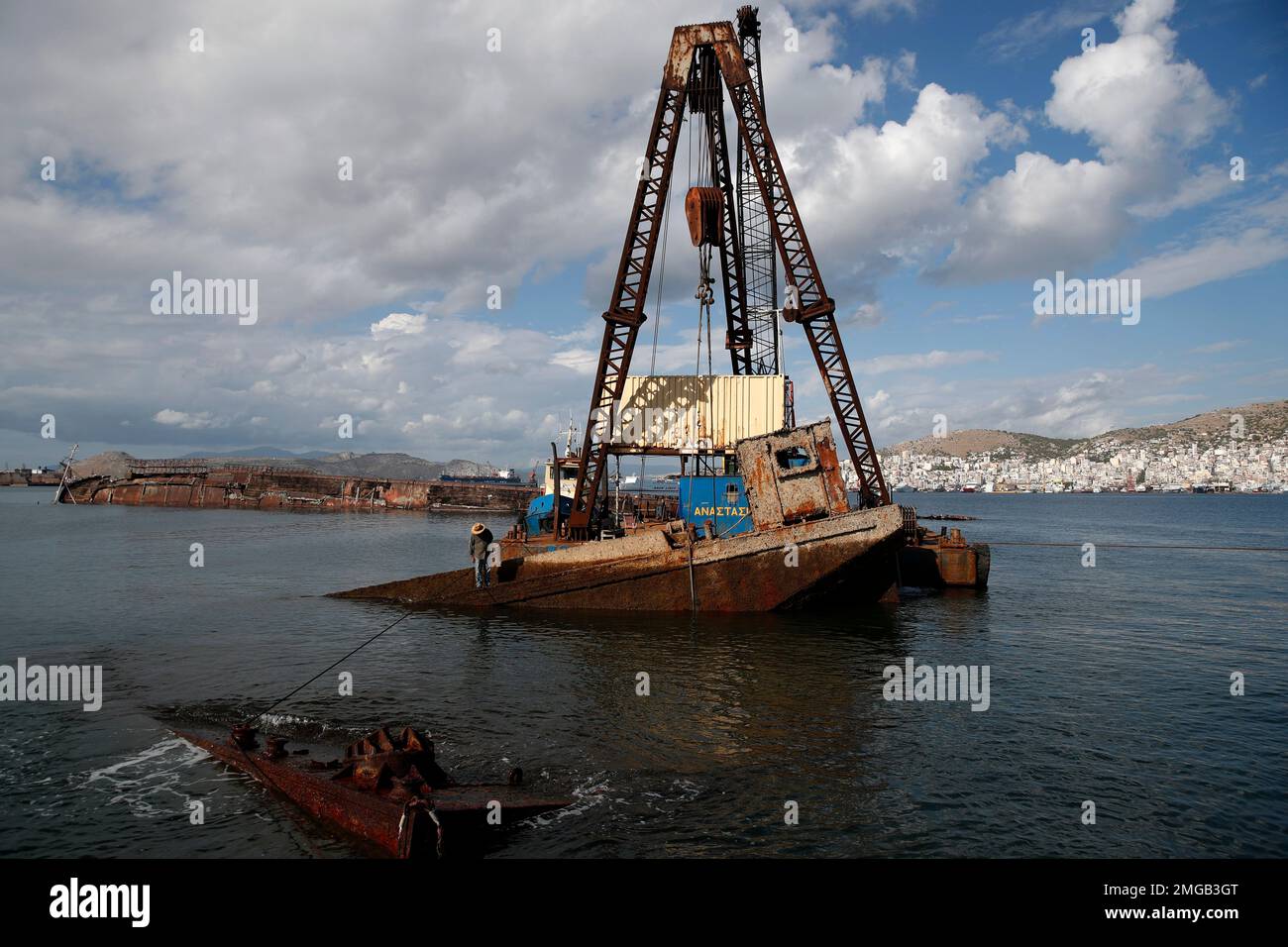 A floating crane holds an old vessel as a worker checks the progress of ...