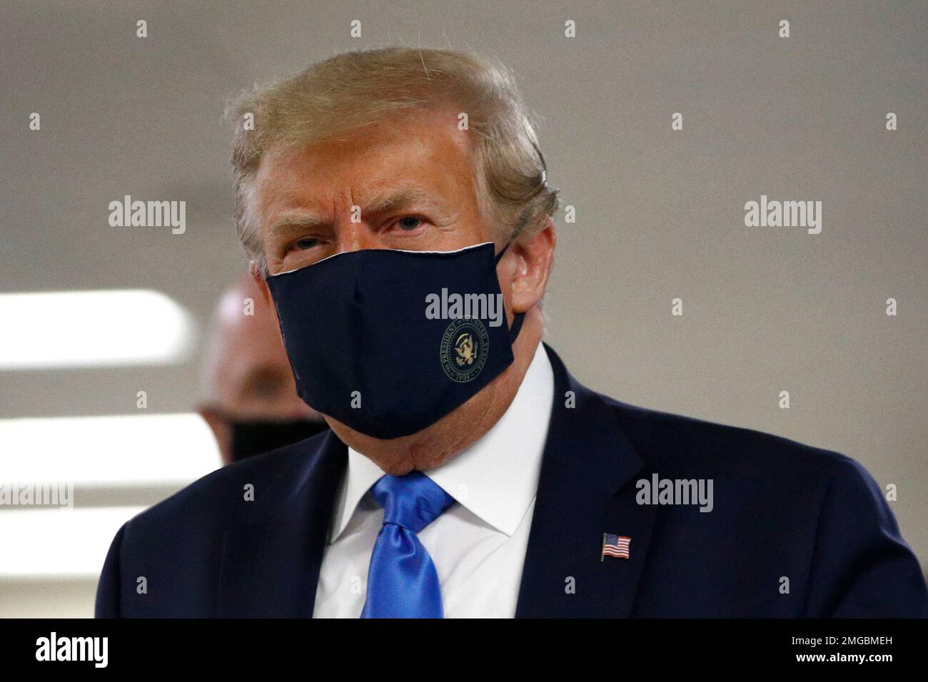 President Donald Trump wears a face mask as he walks down a hallway ...