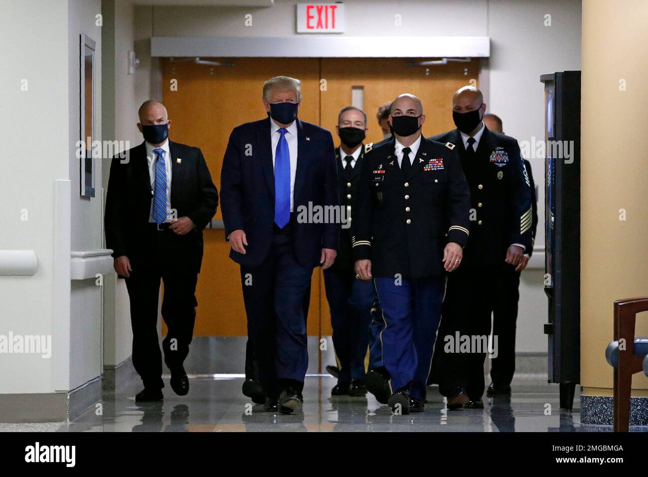 President Donald Trump wears a face mask as he walks down a hallway ...