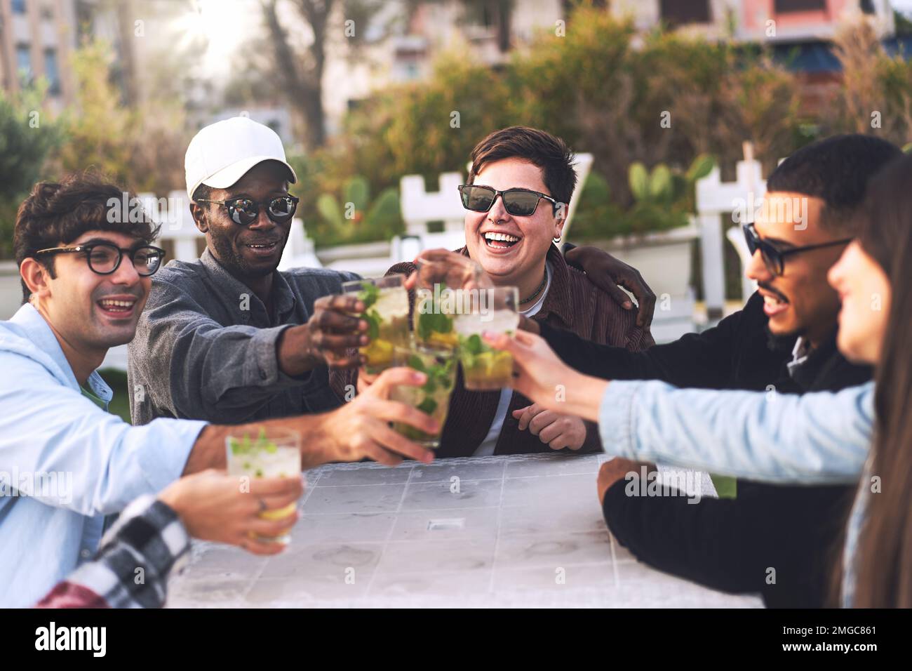 A diverse group of young friends gather around a table at an outdoor ...