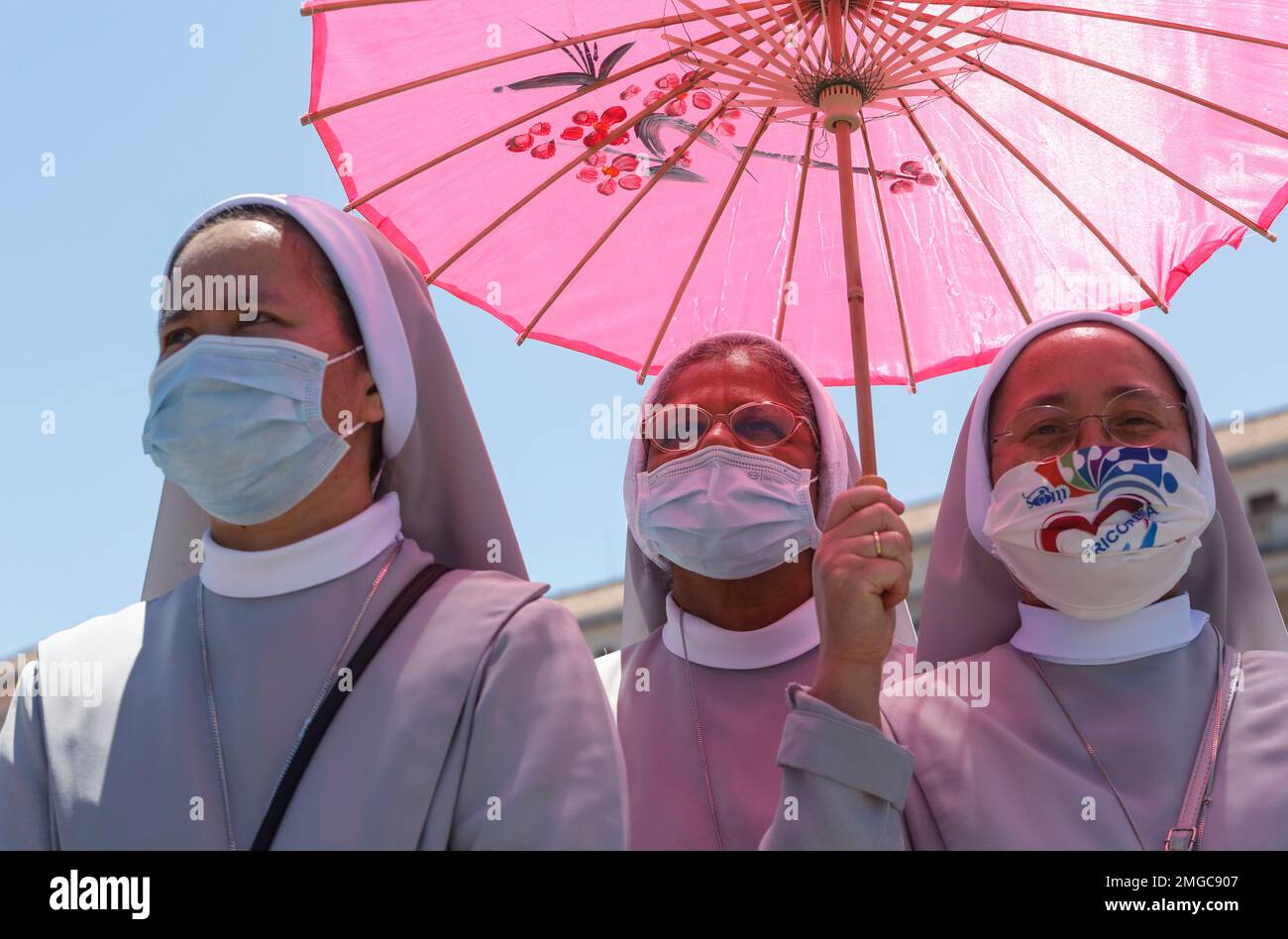 Nuns wearing protective masks take shelter from the sun as they attend ...