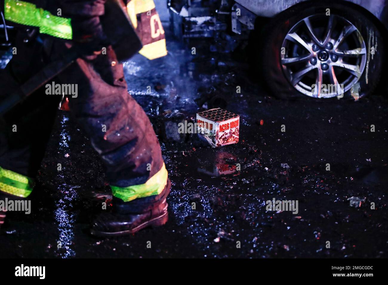 A box of spent fireworks sits on the pavement near two cars which ...