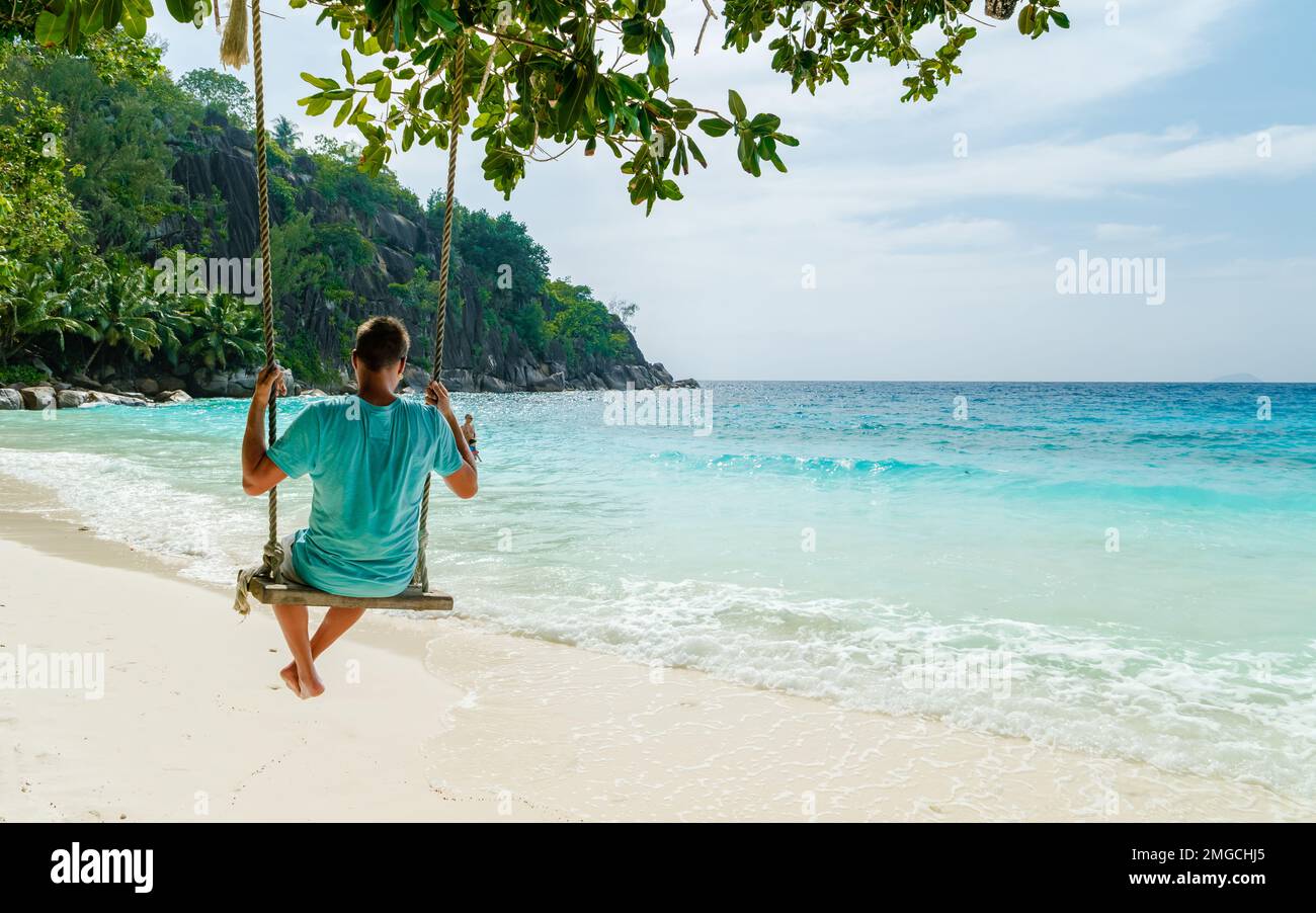 Young men relaxing in a swing on the beach of Mahe Tropical Seychelles ...