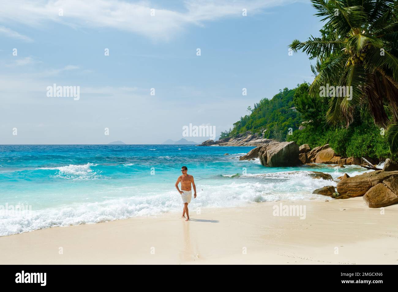 Young men in a swim short on a white tropical beach with palm trees ...