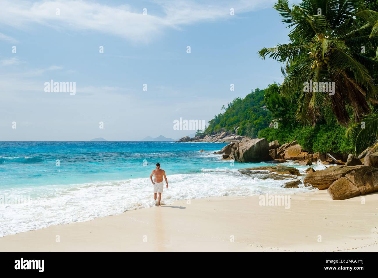 Young men in swim short on a white tropical beach with palm trees ...
